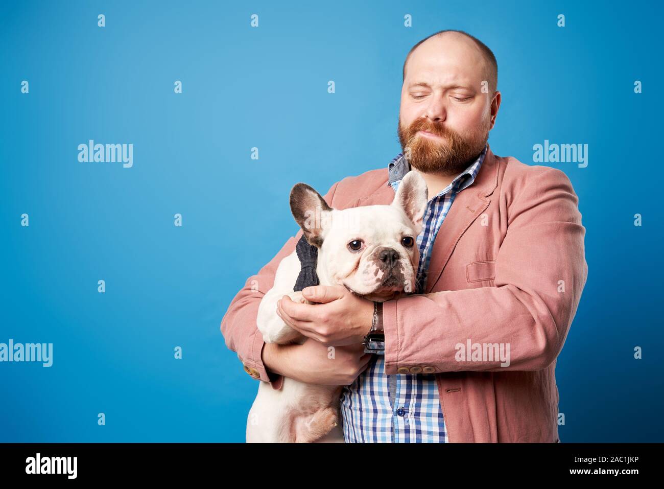 Man with french bulldog in his arms on empty blue background in studio ...