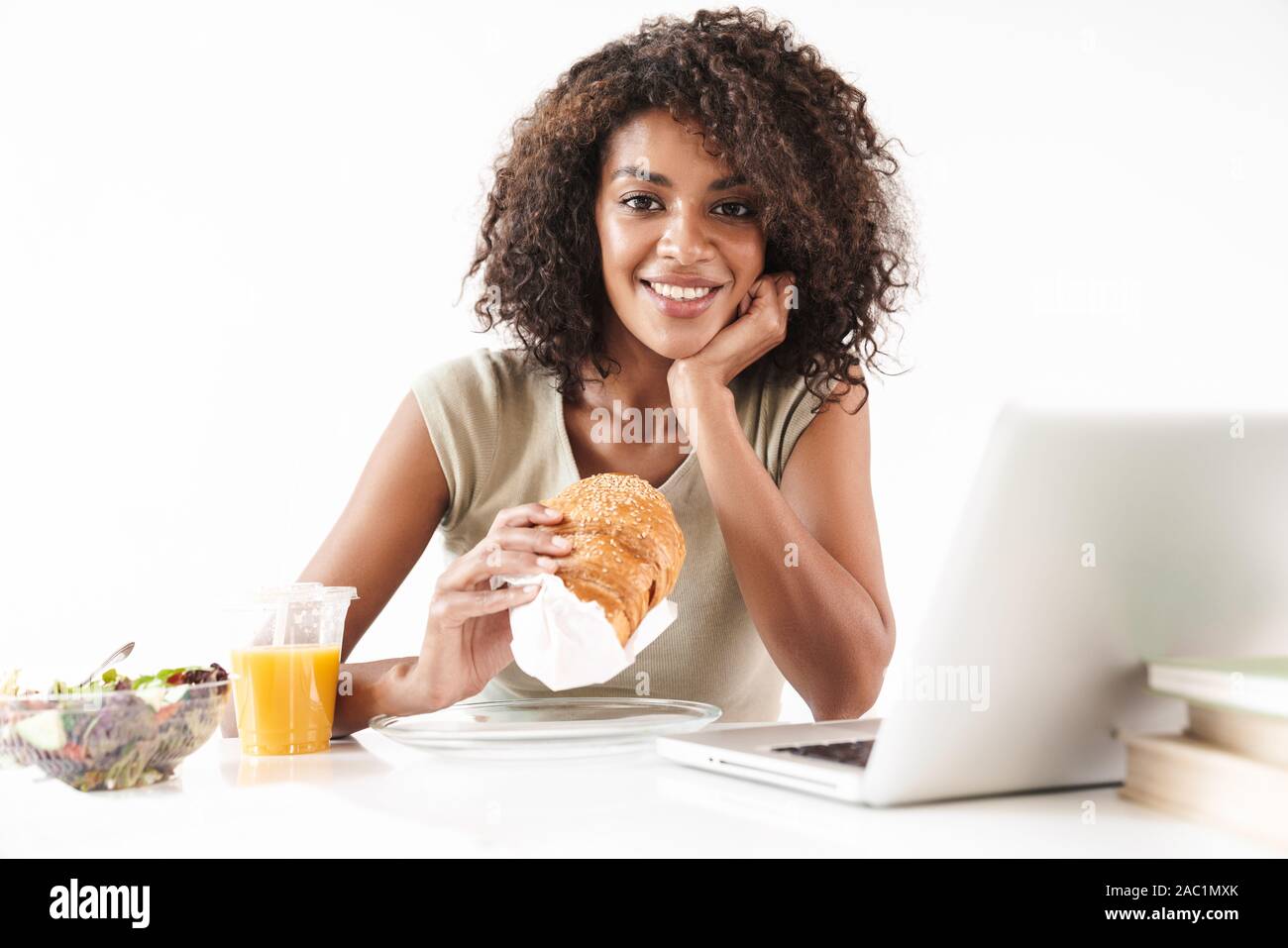 Beautiful smiling young african woman sitting at the desk isolated over ...