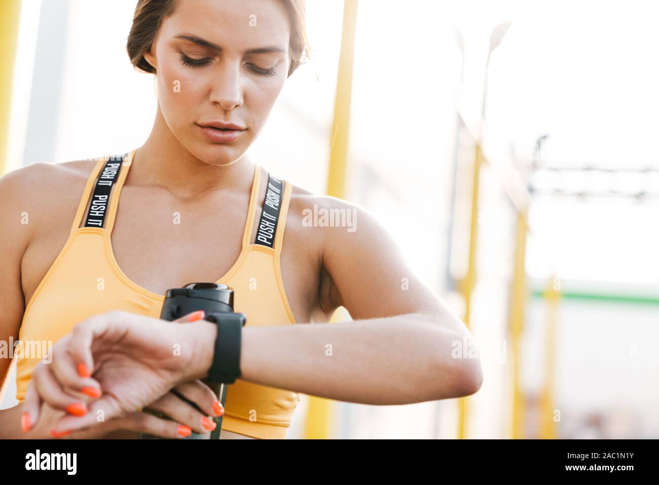 Image of concentrated woman in sportswear looking at smartwatch while ...