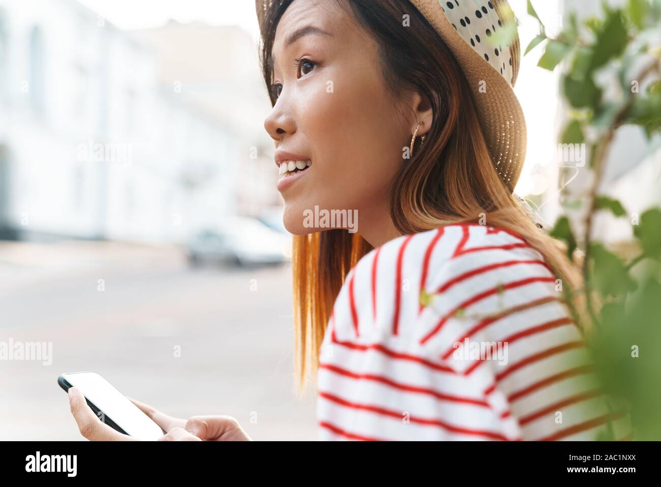 Image of a young positive beautiful asian woman walking outdoors using ...