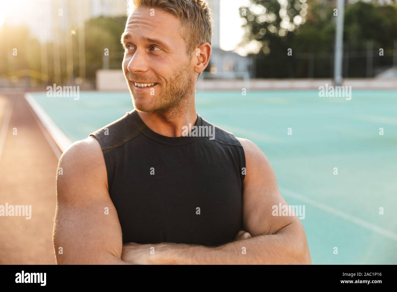 Image of masculine sportsman smiling and standing at stadium while ...