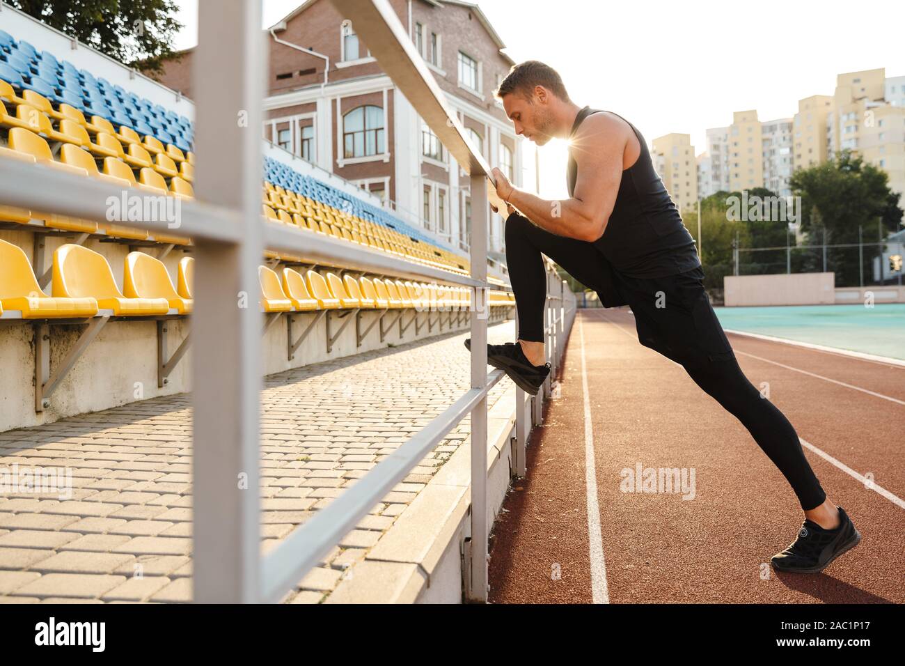 Photo of strong young sports man make stretching exercises at stadium ...