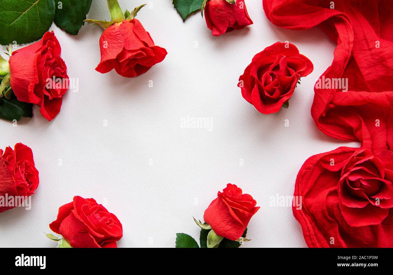 Red roses heads ans scarf scattered on a white background, overhead ...