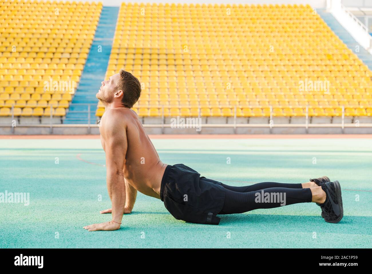 Image of athletic shirtless man stretching his body at sports stadium ...