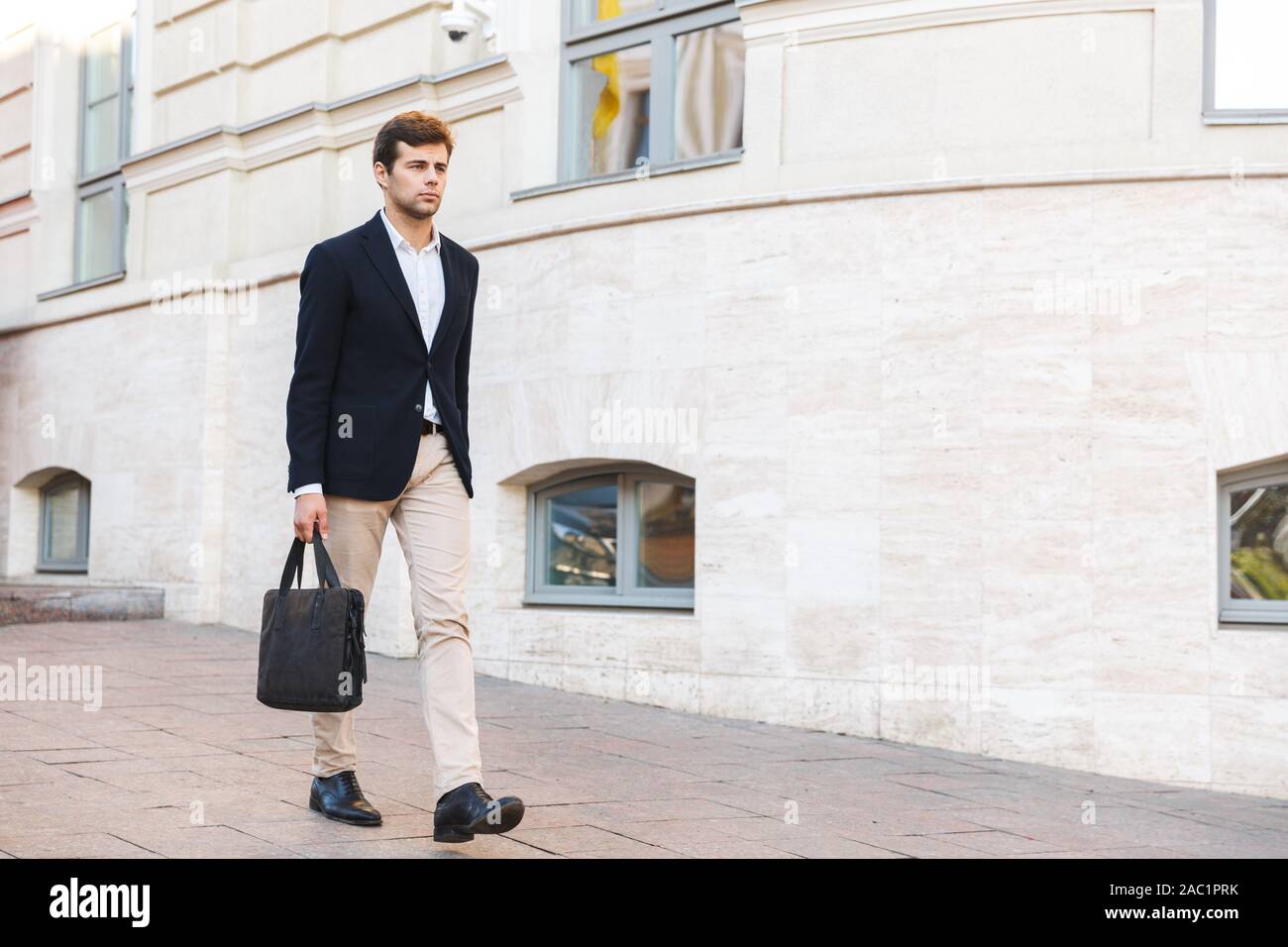 Photo of serious young businessman in suit walking on city street and ...