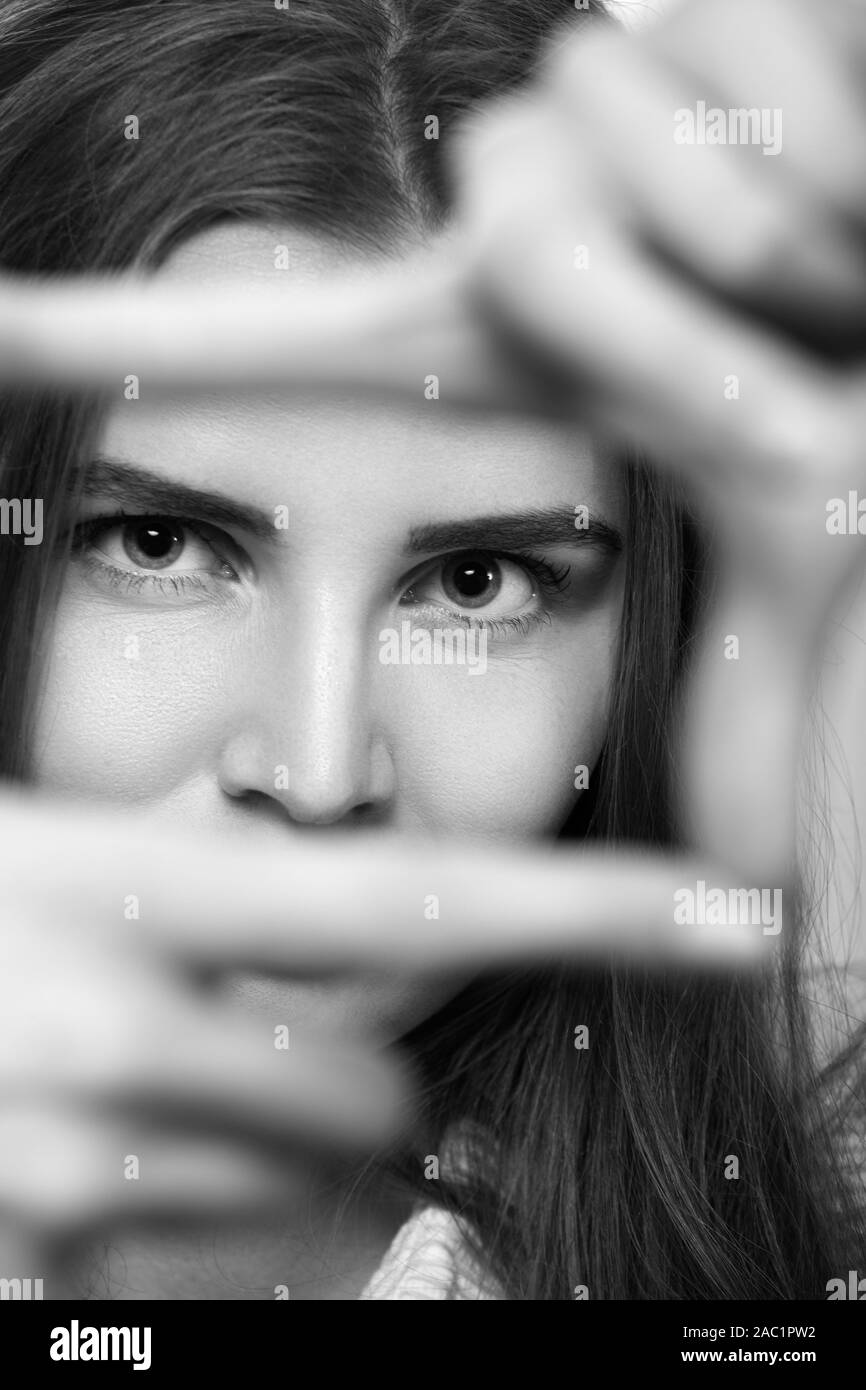 young woman looking at camera through fingers frame gesture closeup ...