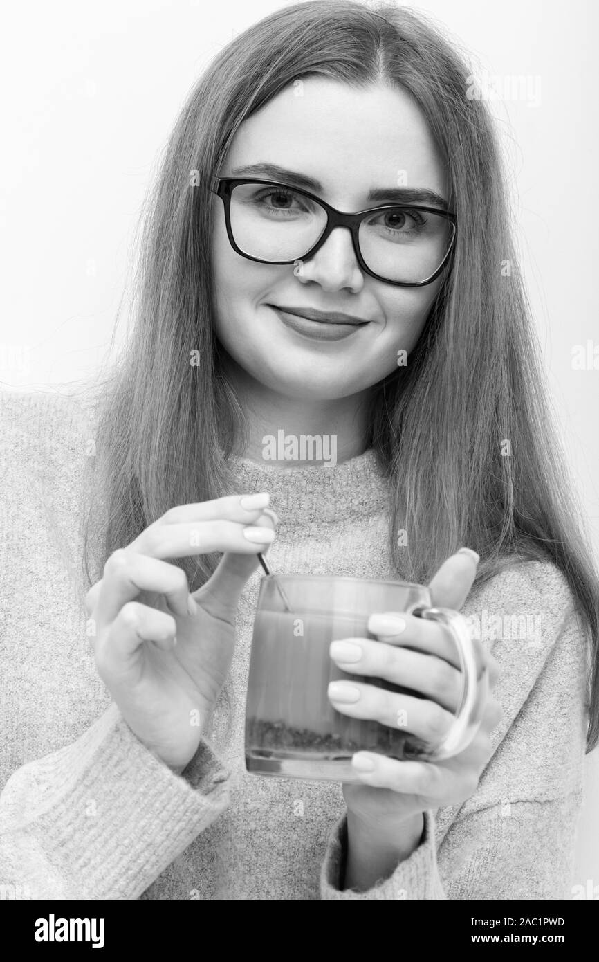 young woman in eyeglasses sitting on white background with mug of tea ...