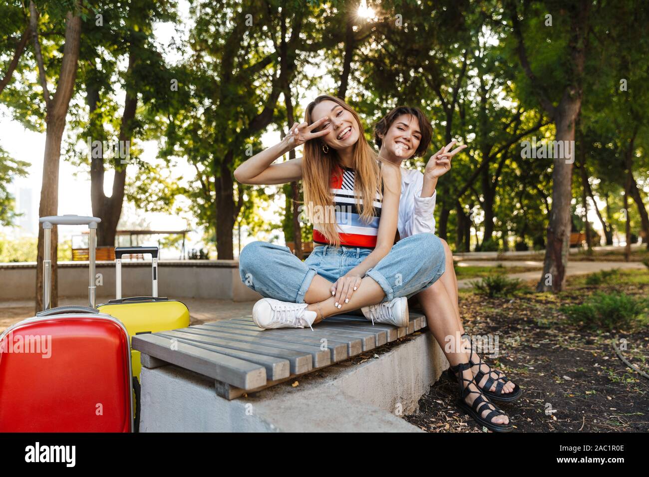 Photo of two delighted tourist women showing peace sign while sitting ...