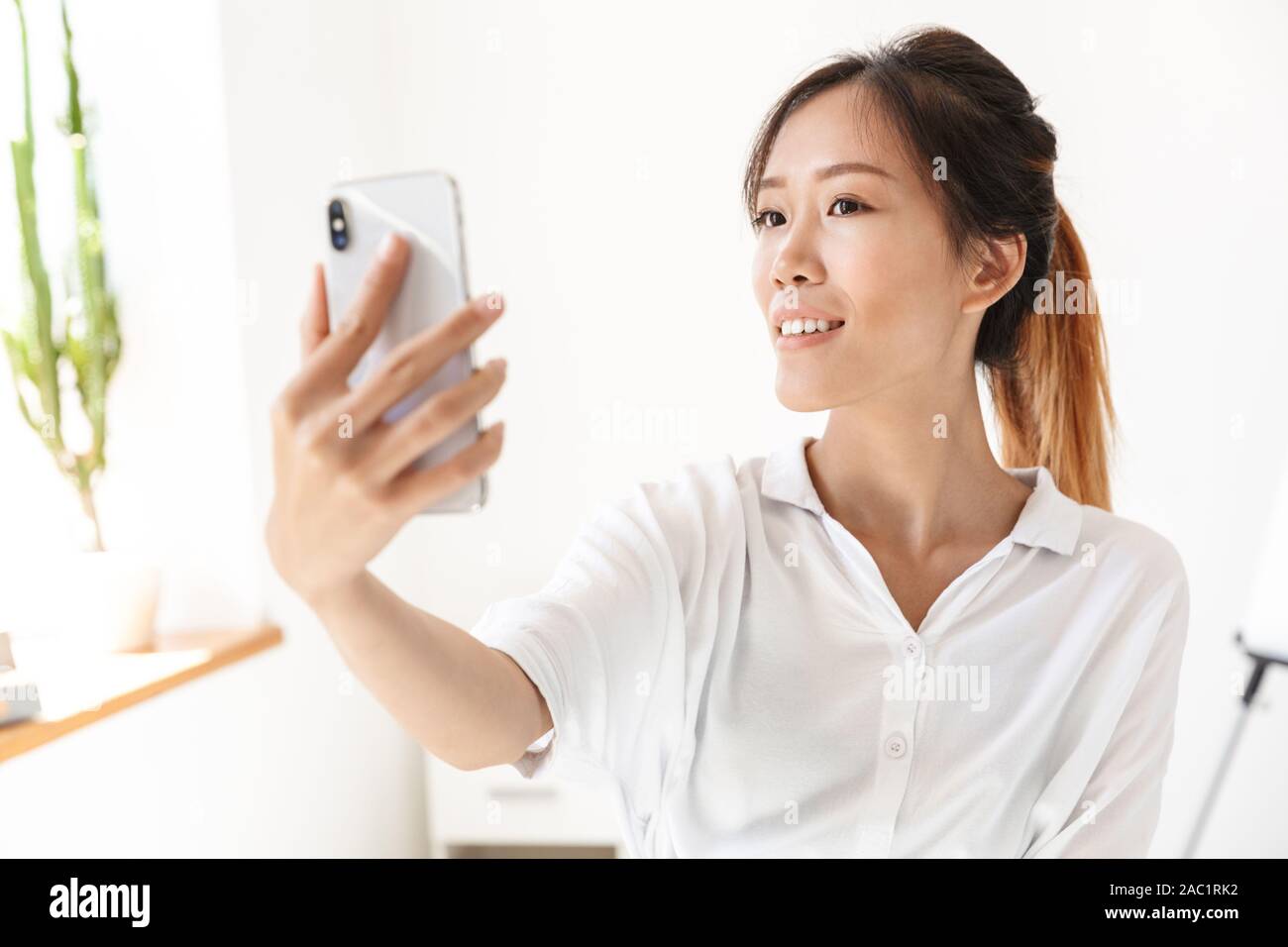 Smiling lovely young asian businsswoman taking a selfie while standing ...