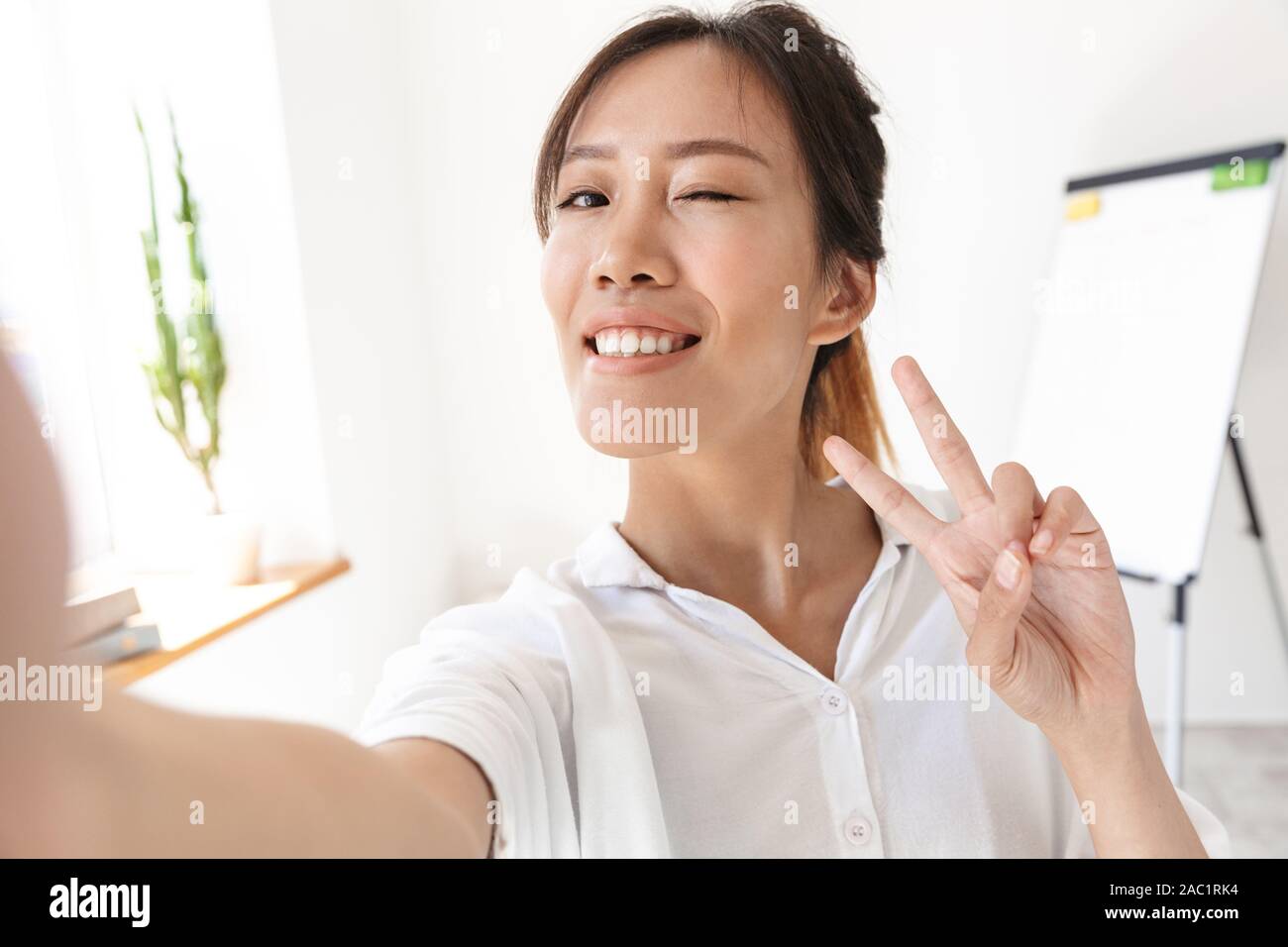 Smiling lovely young asian businsswoman taking a selfie while standing ...