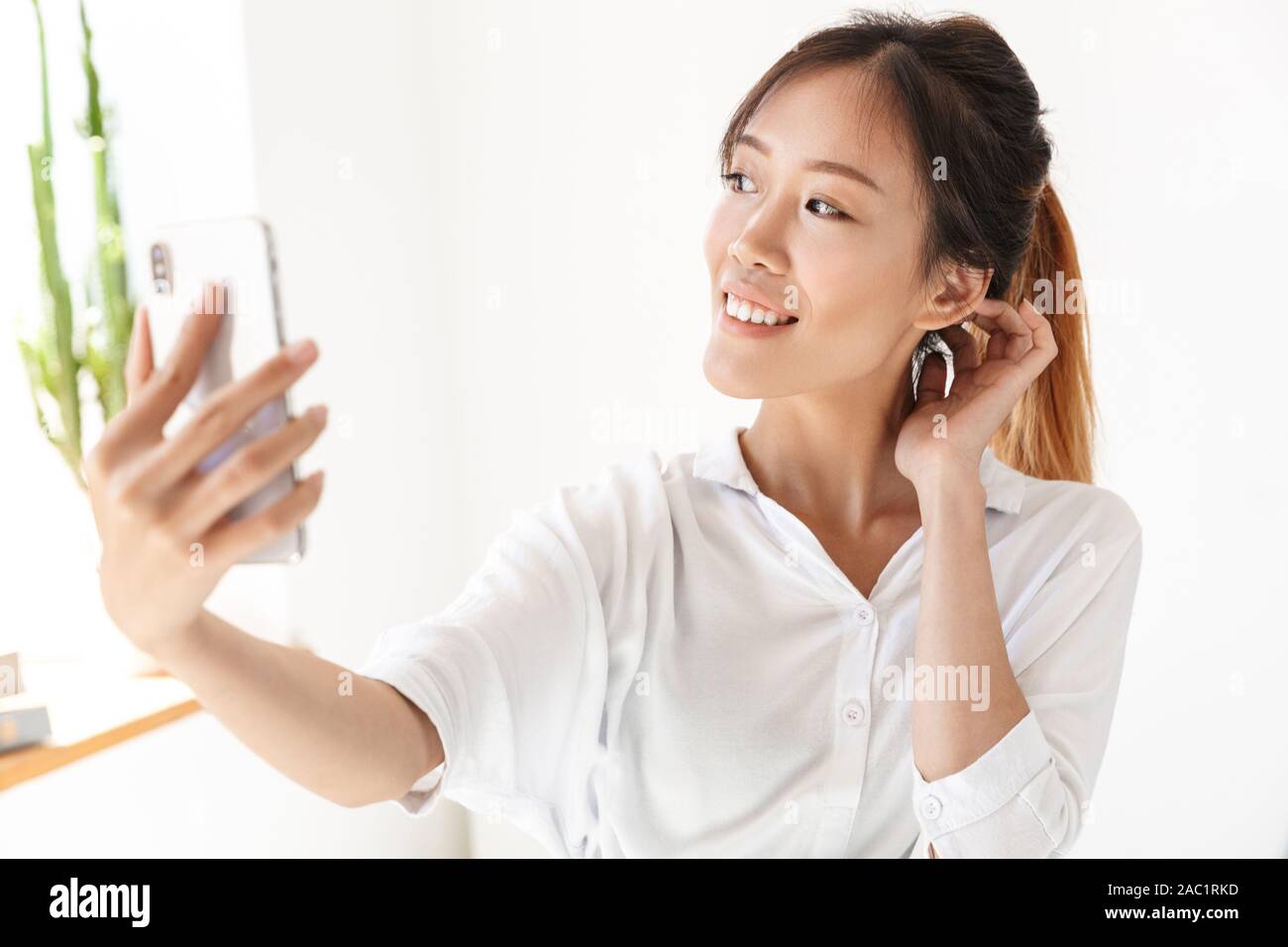 Smiling lovely young asian businsswoman taking a selfie while standing ...