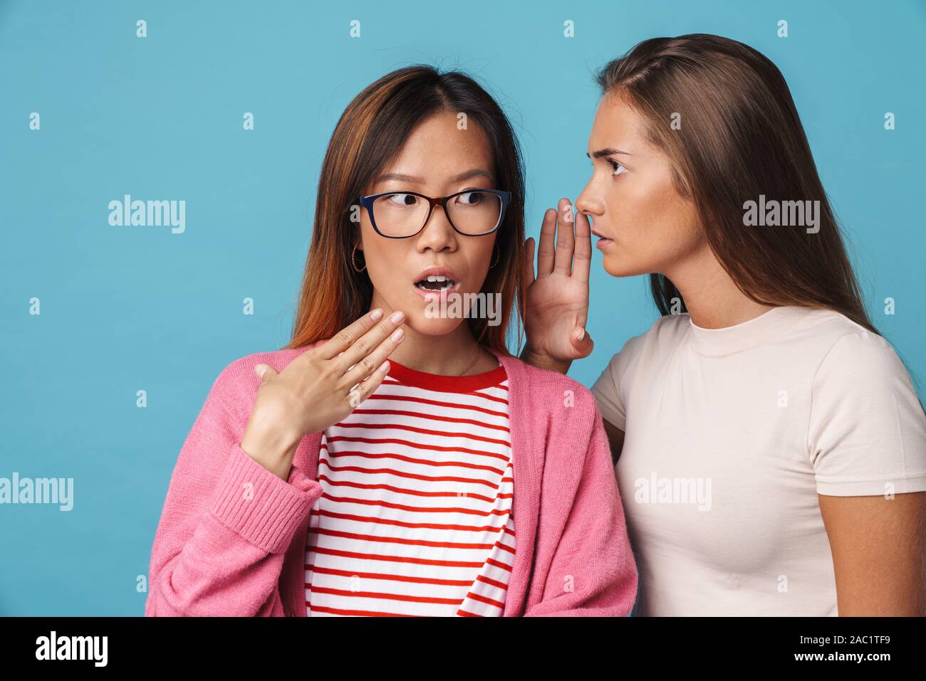 Portrait of two multinational young women in casual clothes whispering ...