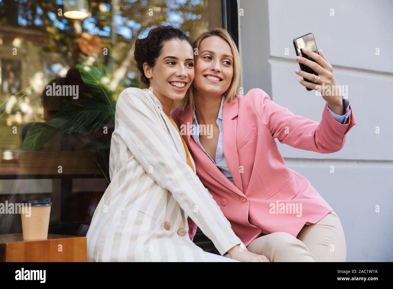 Image of a positive two business women colleagues outdoors using mobile ...