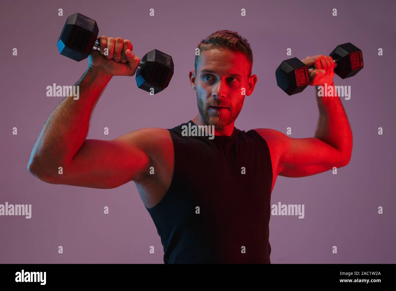 Photo of a handsome young sports man posing isolated over neon lights ...