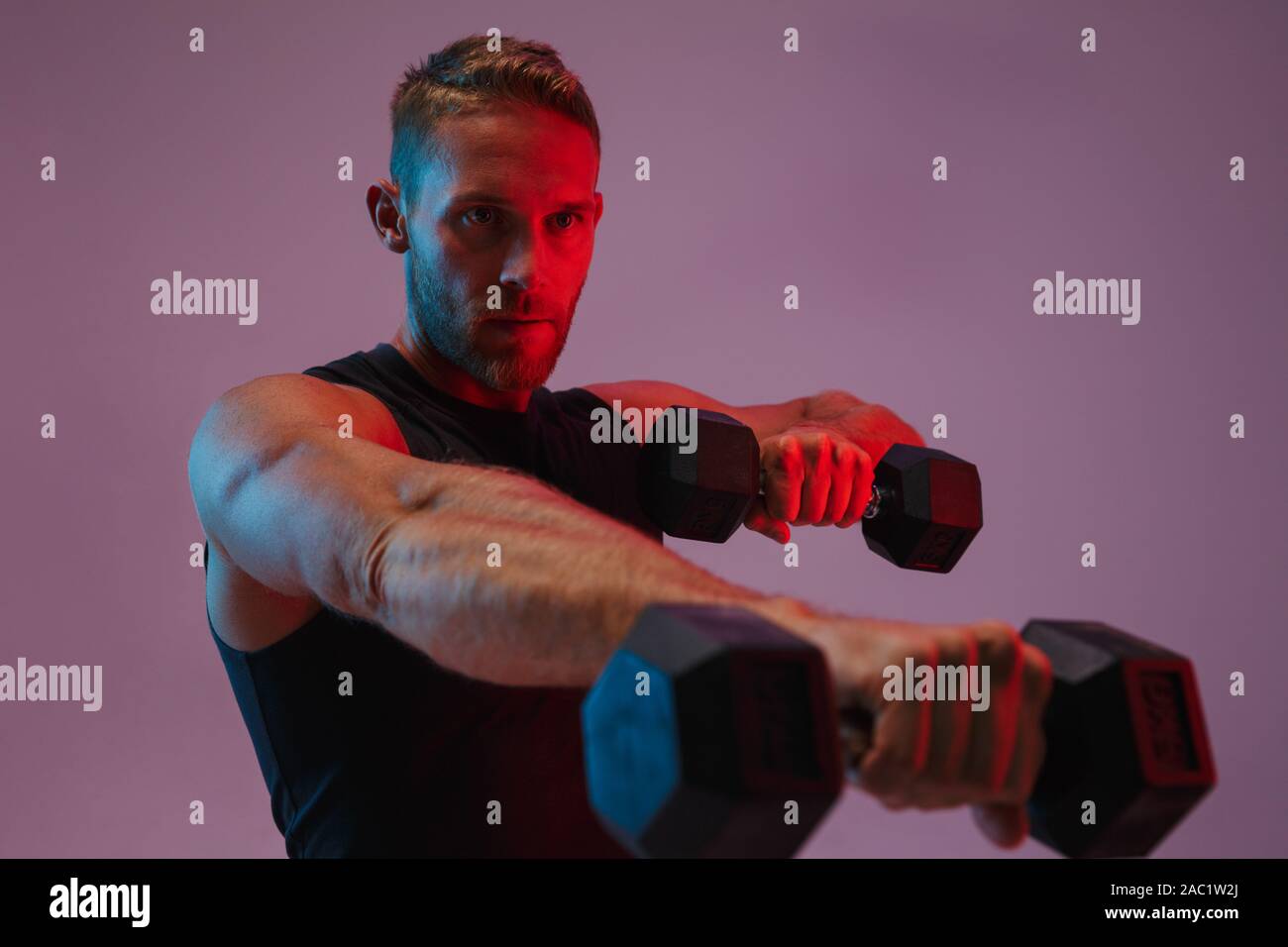 Photo of a serious young sports man posing isolated over neon lights ...