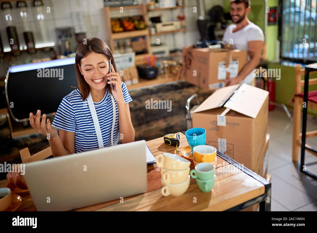 Woman having happy conversation over the phone while man unpacks boxes ...