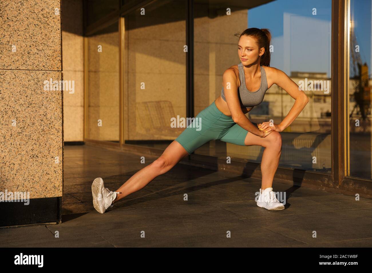 Attractive fit young sportsgirl doing stretching exercises standing ...