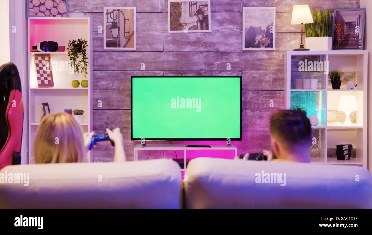 Young couple sitting on sofa and playing online games on tv with green ...