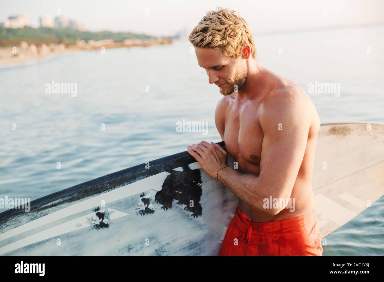 Photo of a strong handsome man surfer with surfing desk at the beach ...
