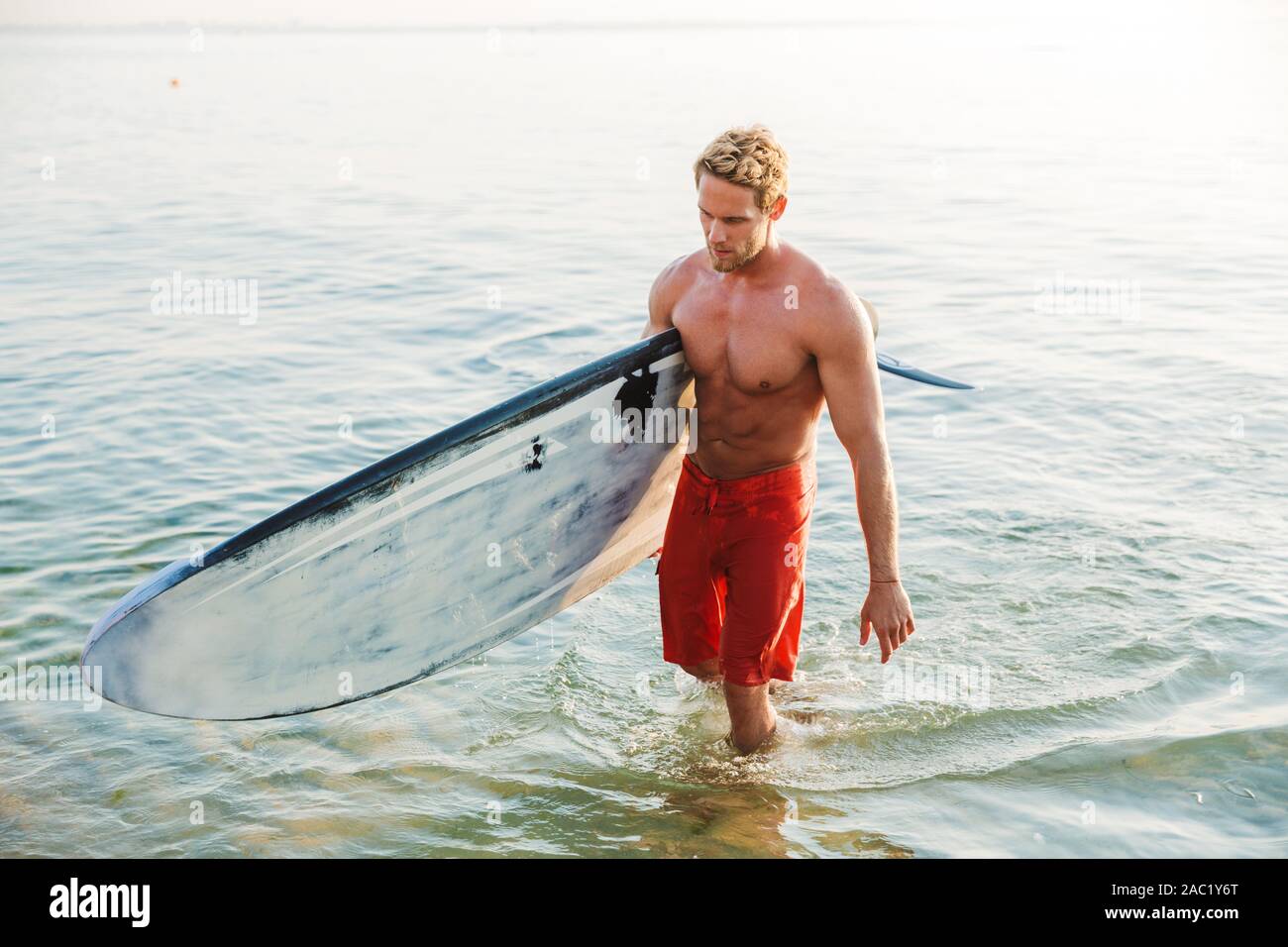 Photo of a strong concentrated handsome young man surfer with surfing ...