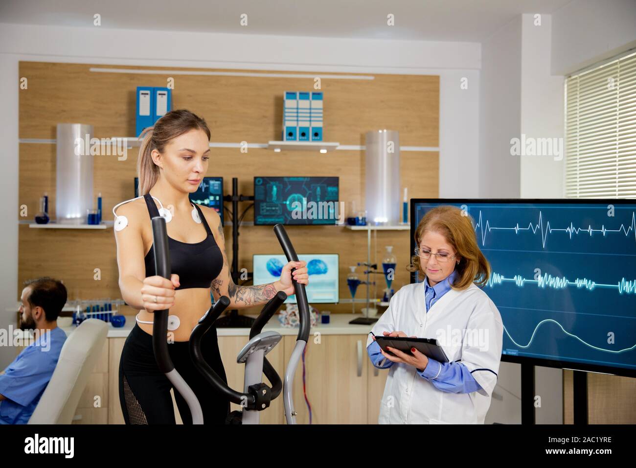 Female athlete running tests on the stepper and doctor making notes in ...