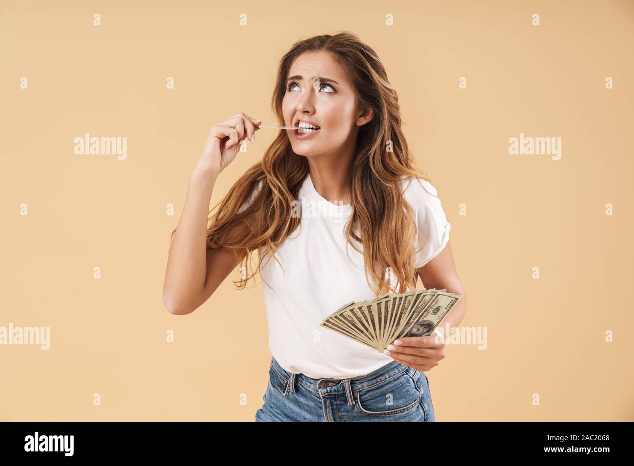 Portrait of amazed woman biting credit card and holding cash money ...