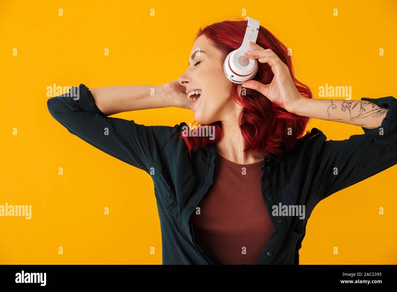 Image of young cheerful woman with curly red hair listening music with ...