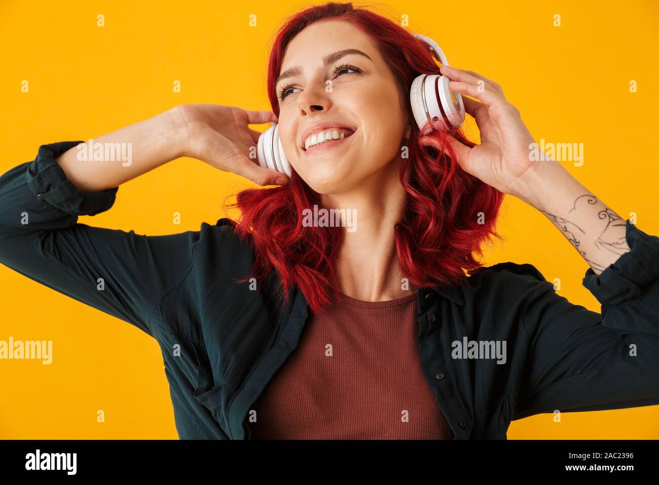 Image of young smiling woman with curly red hair listening music with ...