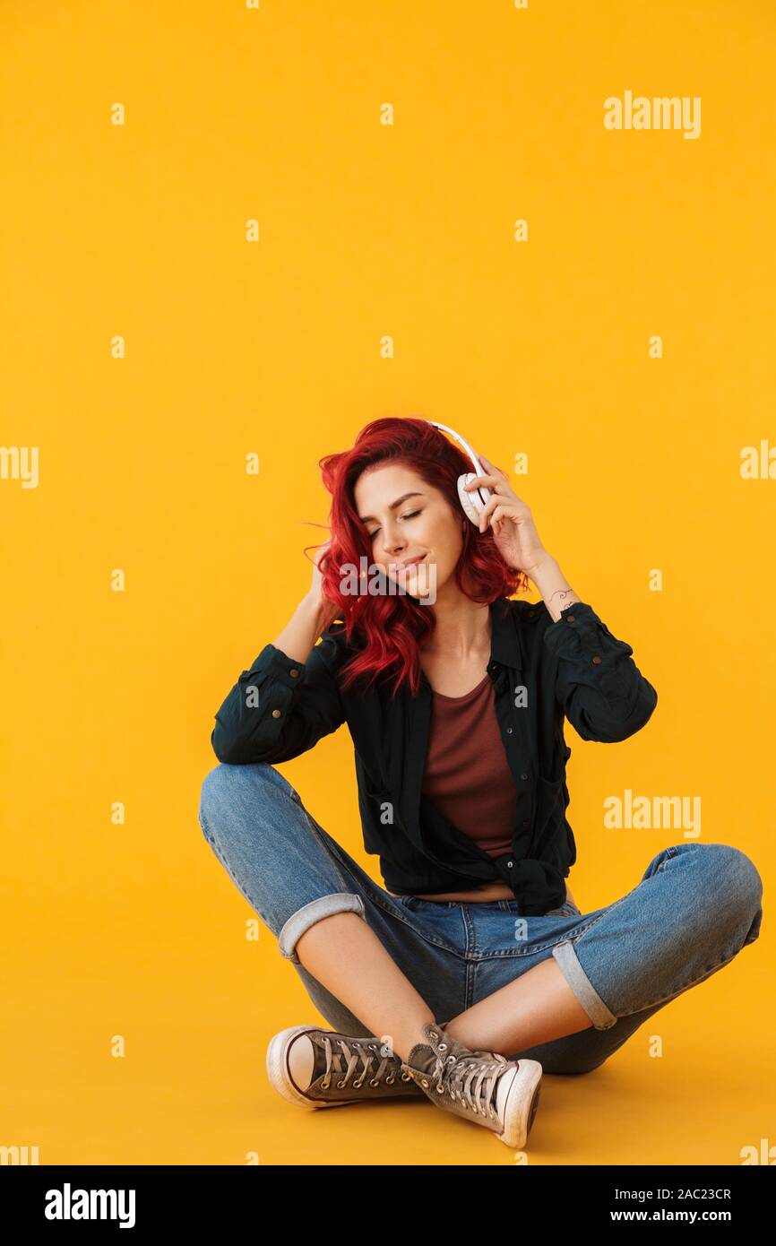 Image of pleased cute woman with curly red hair using headphones while ...