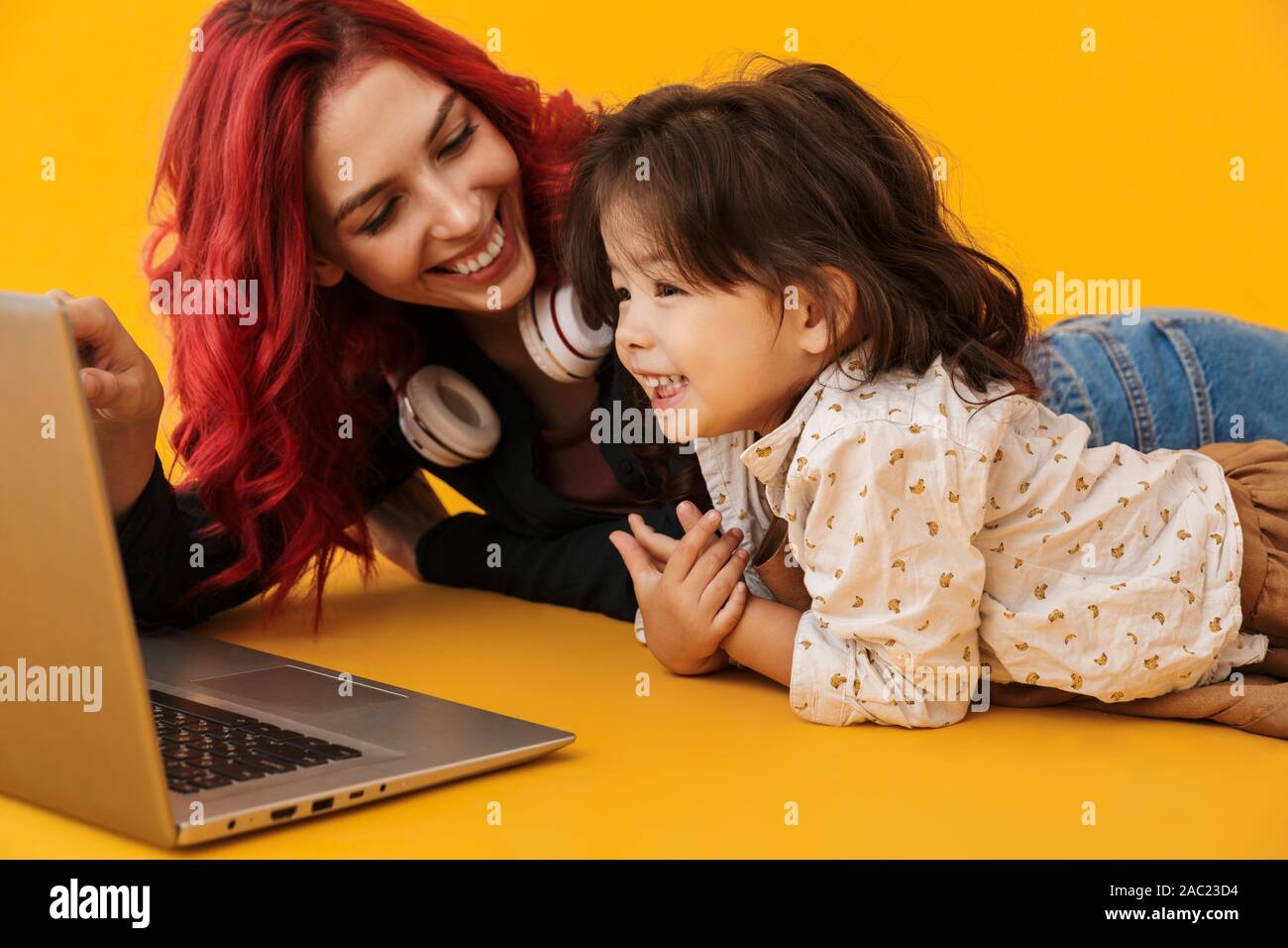 Image of smiling lovely woman and her daughter using laptop while lying ...