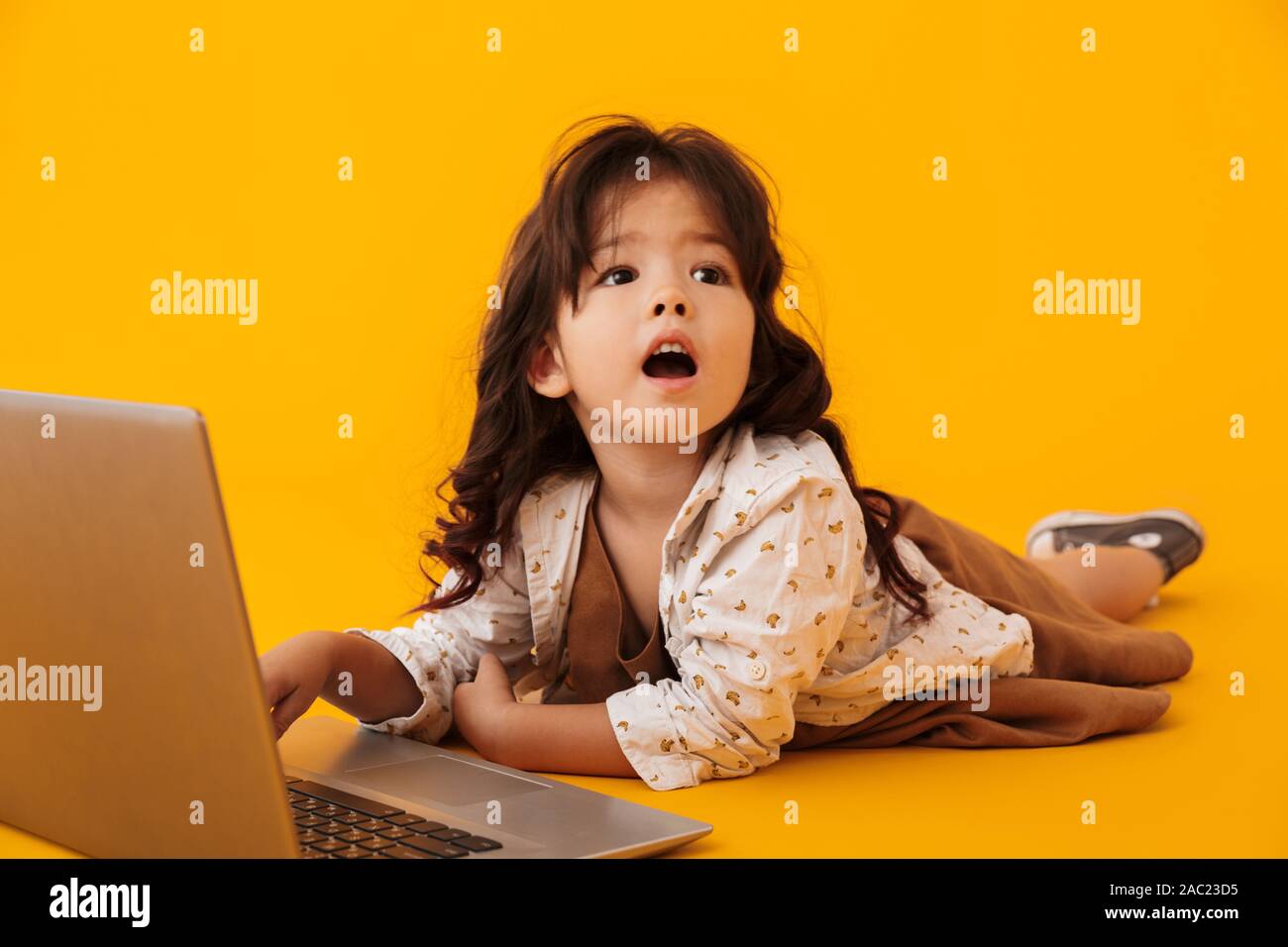 Image of amazed nice girl typing on laptop while lying on floor ...