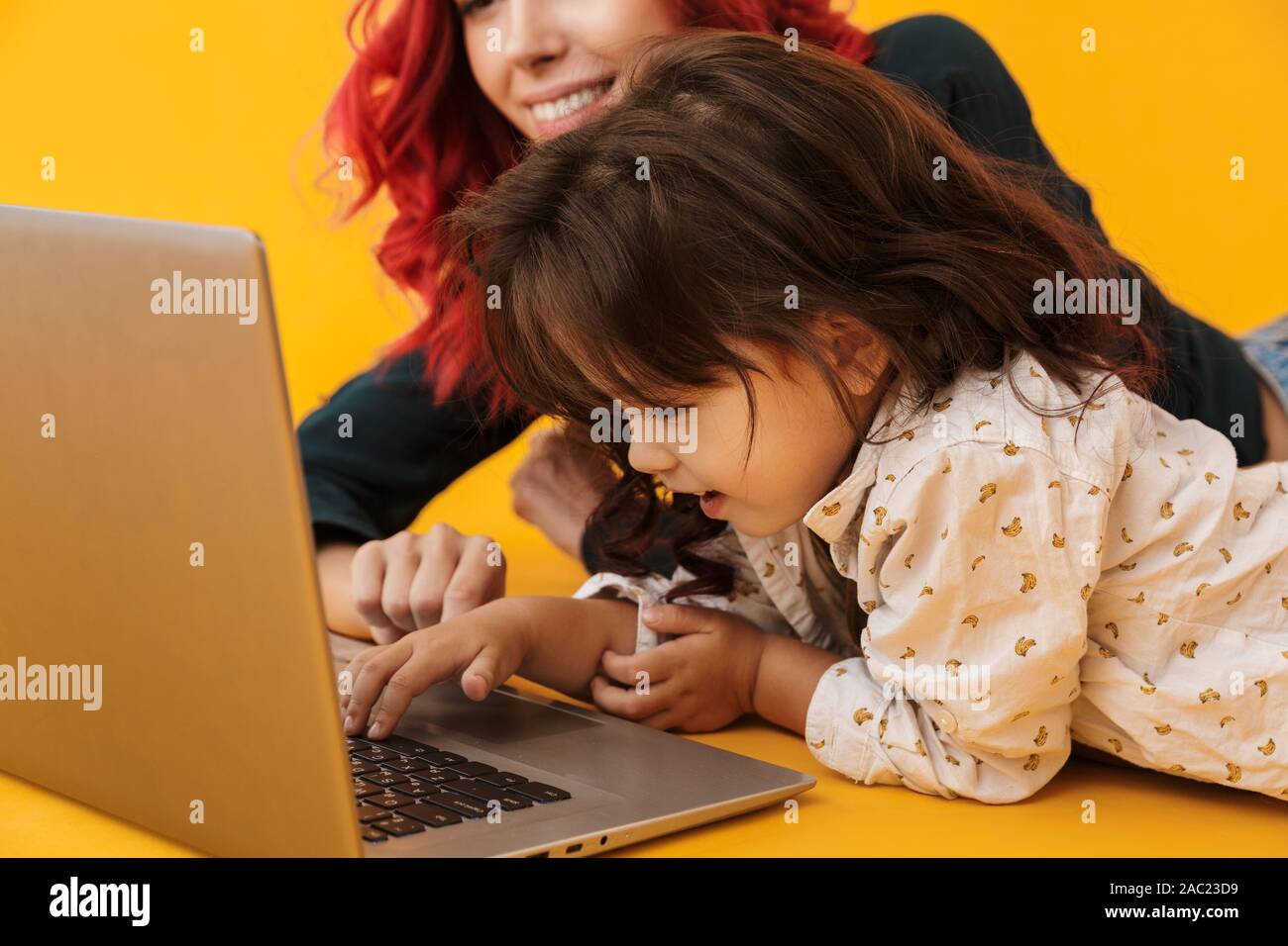 Image of smiling pretty woman and her daughter typing on laptop while ...