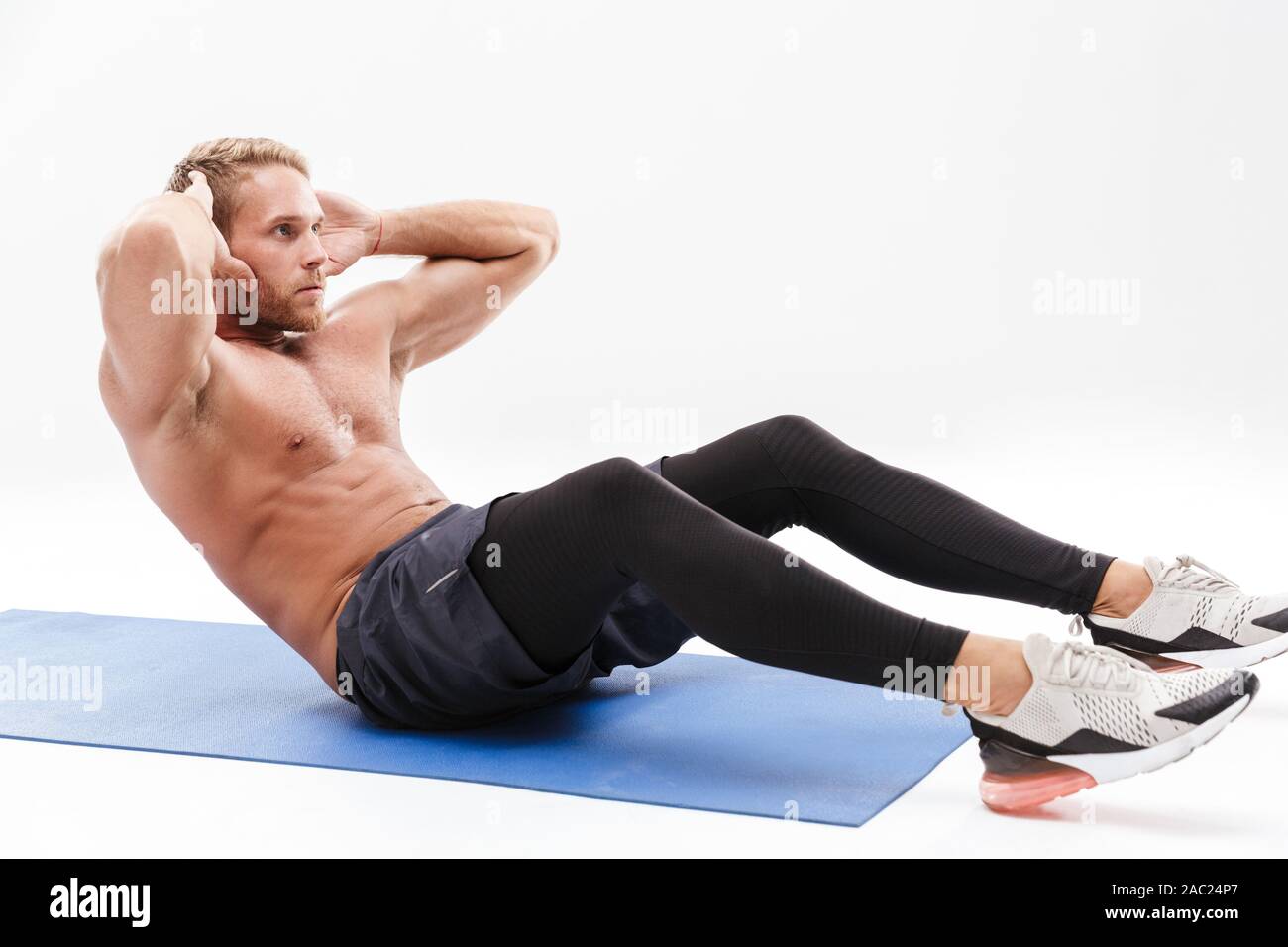 Confident attractive sportsman doing crunches on a fitness mat isolated ...