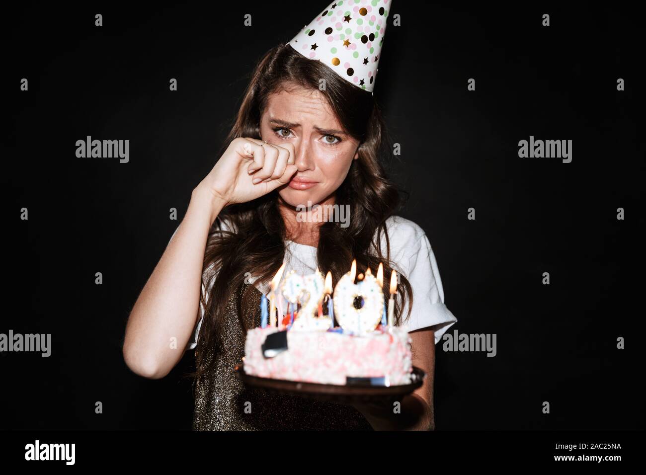 Image of beautiful upset woman in party cone holding cake with candles ...