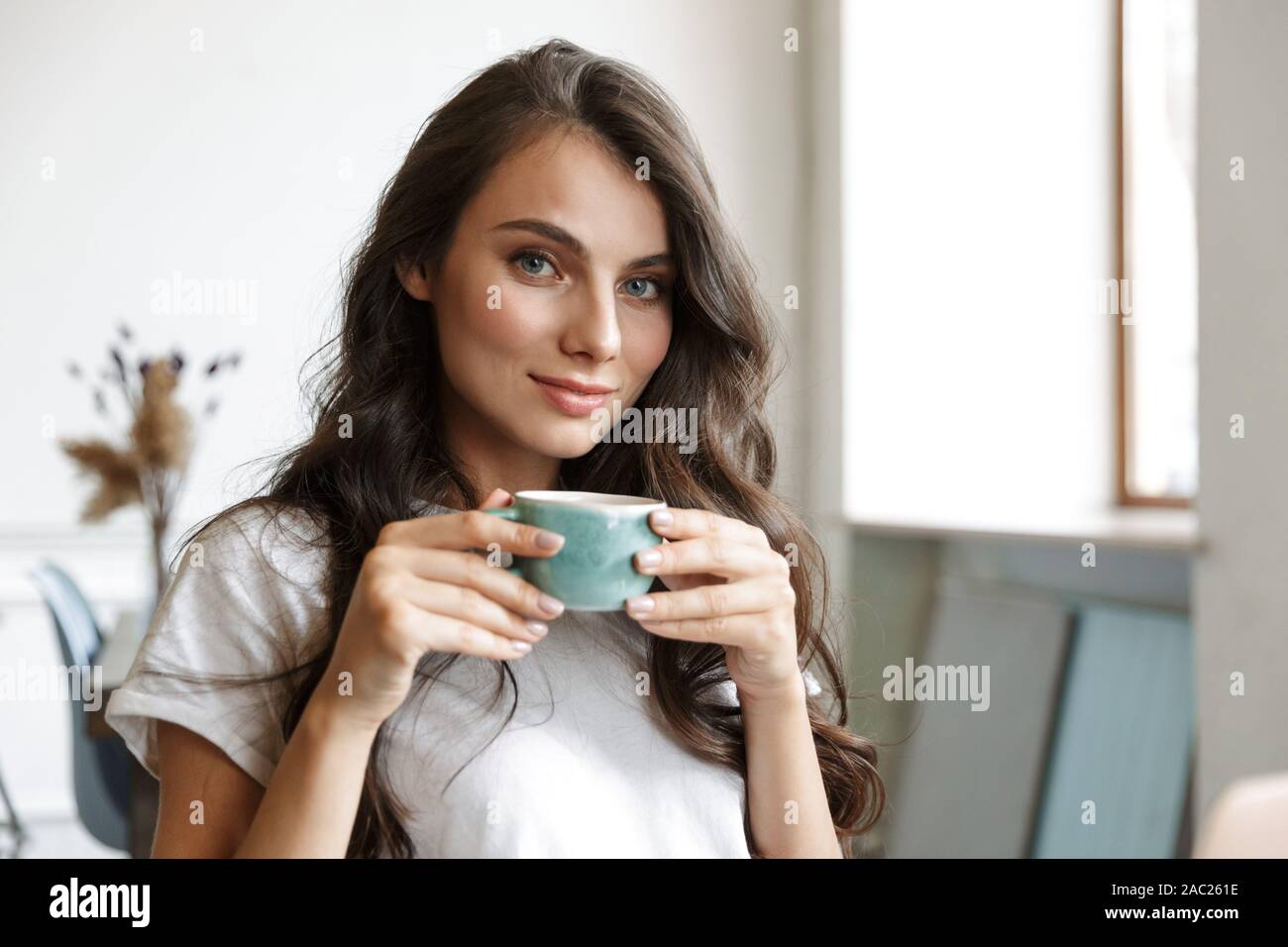 Image of a beautiful optimistic young woman indoors at home drinking ...