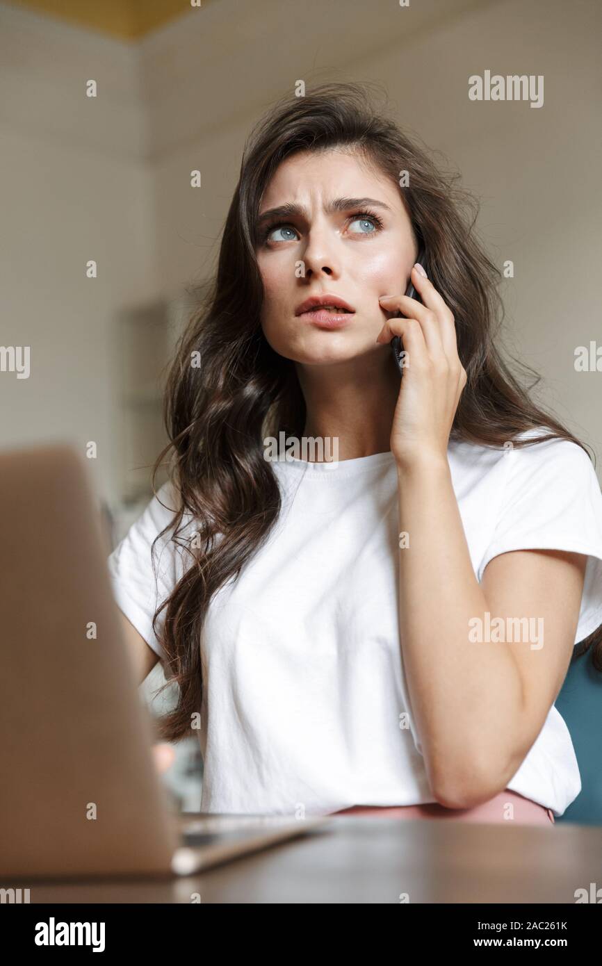 Photo of a confused young woman indoors at home using laptop computer ...