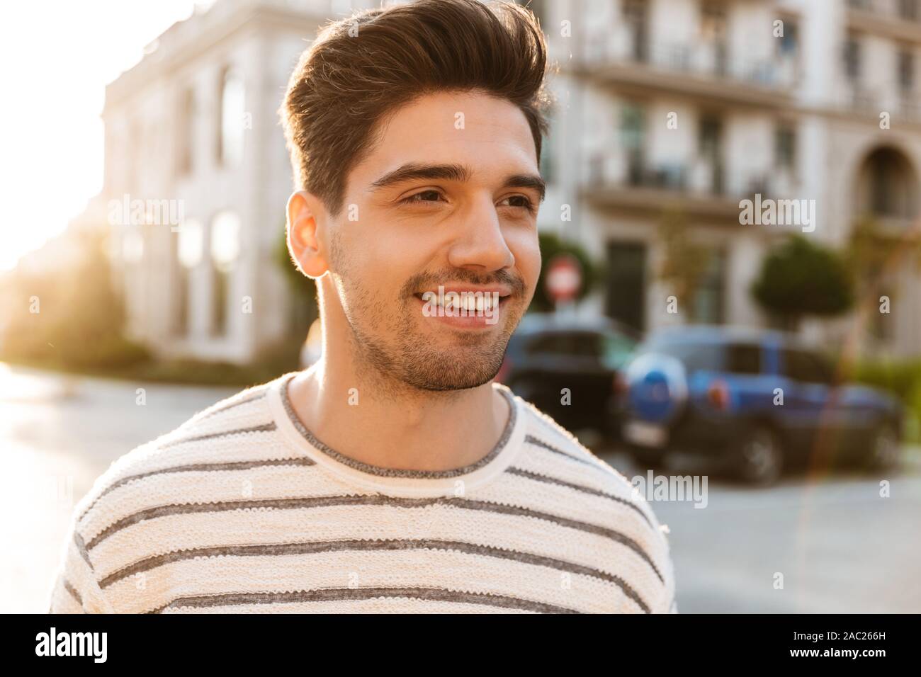 Image of pleased masculine man smiling and looking aside while walking ...
