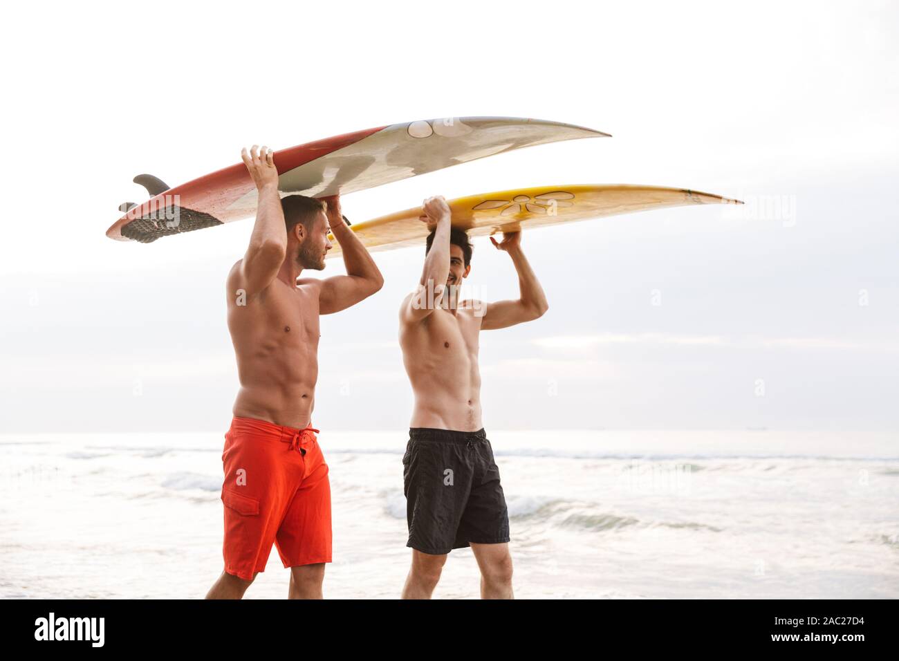 Image of optimistic smiling young two men surfers friends with surfings ...