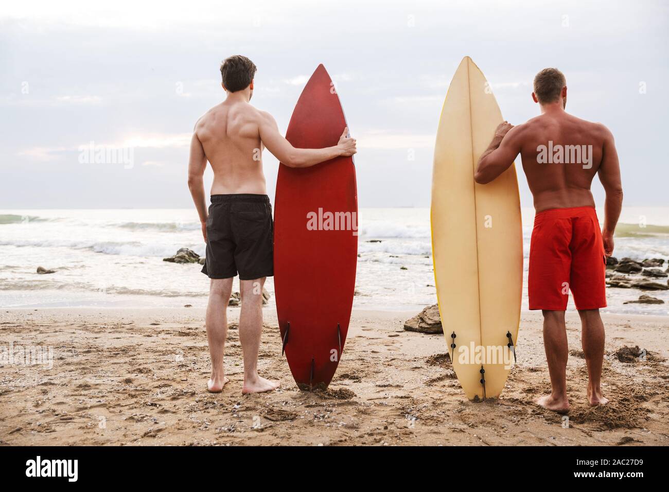 Back view image of a young two men surfers friends with surfings on a ...