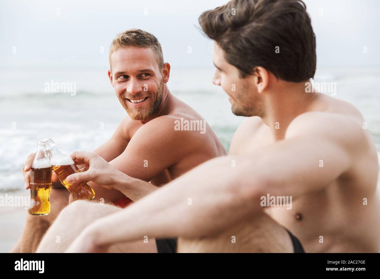 Image of a pleased happy two men surfers friends on a beach outside talking with each other ...
