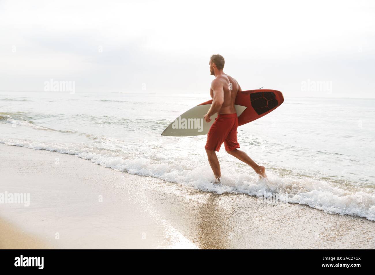 Image of a serious strong handsome man surfer with surfing on a beach ...