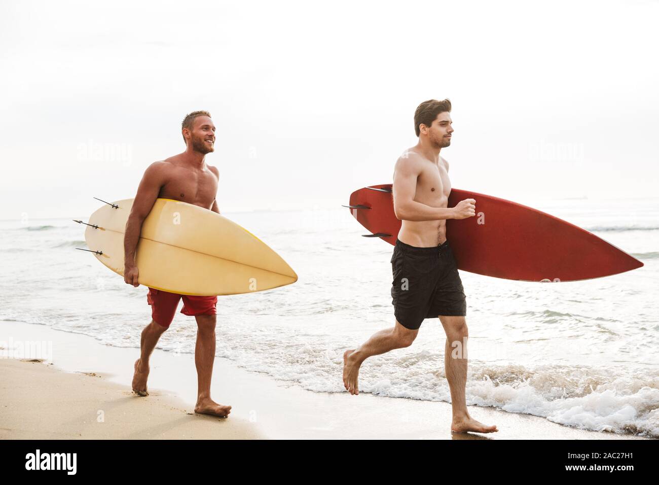 Photo of a young two men surfers friends with surfings on a beach ...