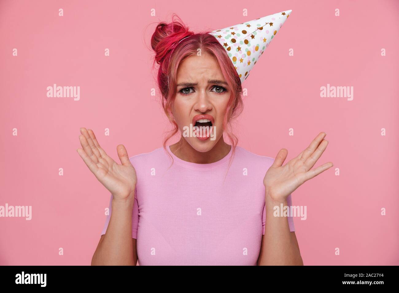Portrait of irritated young woman wearing party cone screaming and ...