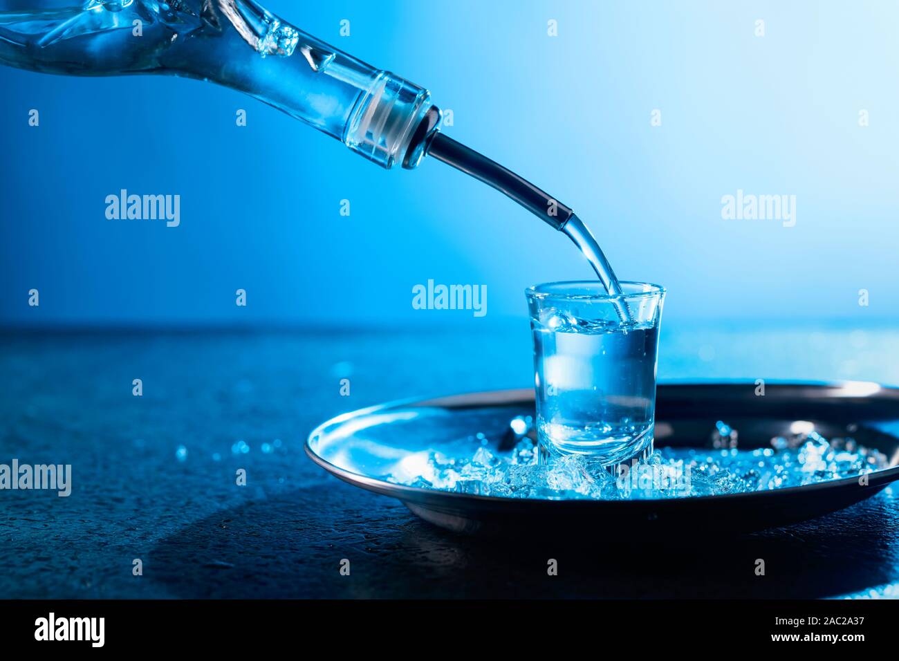 Vodka poured into a glass lit with blue backlight. Copy space. Chilled ...