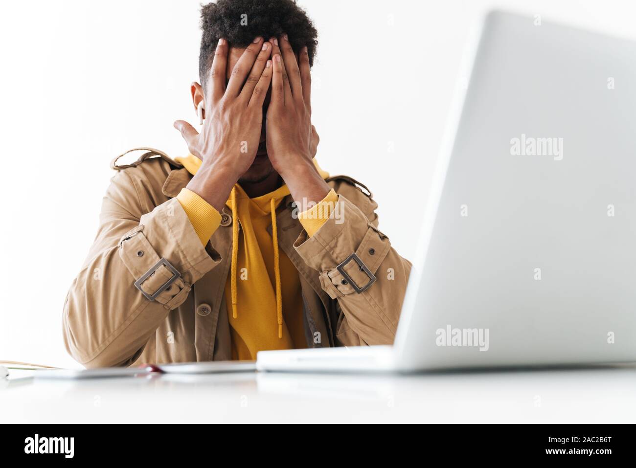Image of upset african american man grabbing his face while working on ...