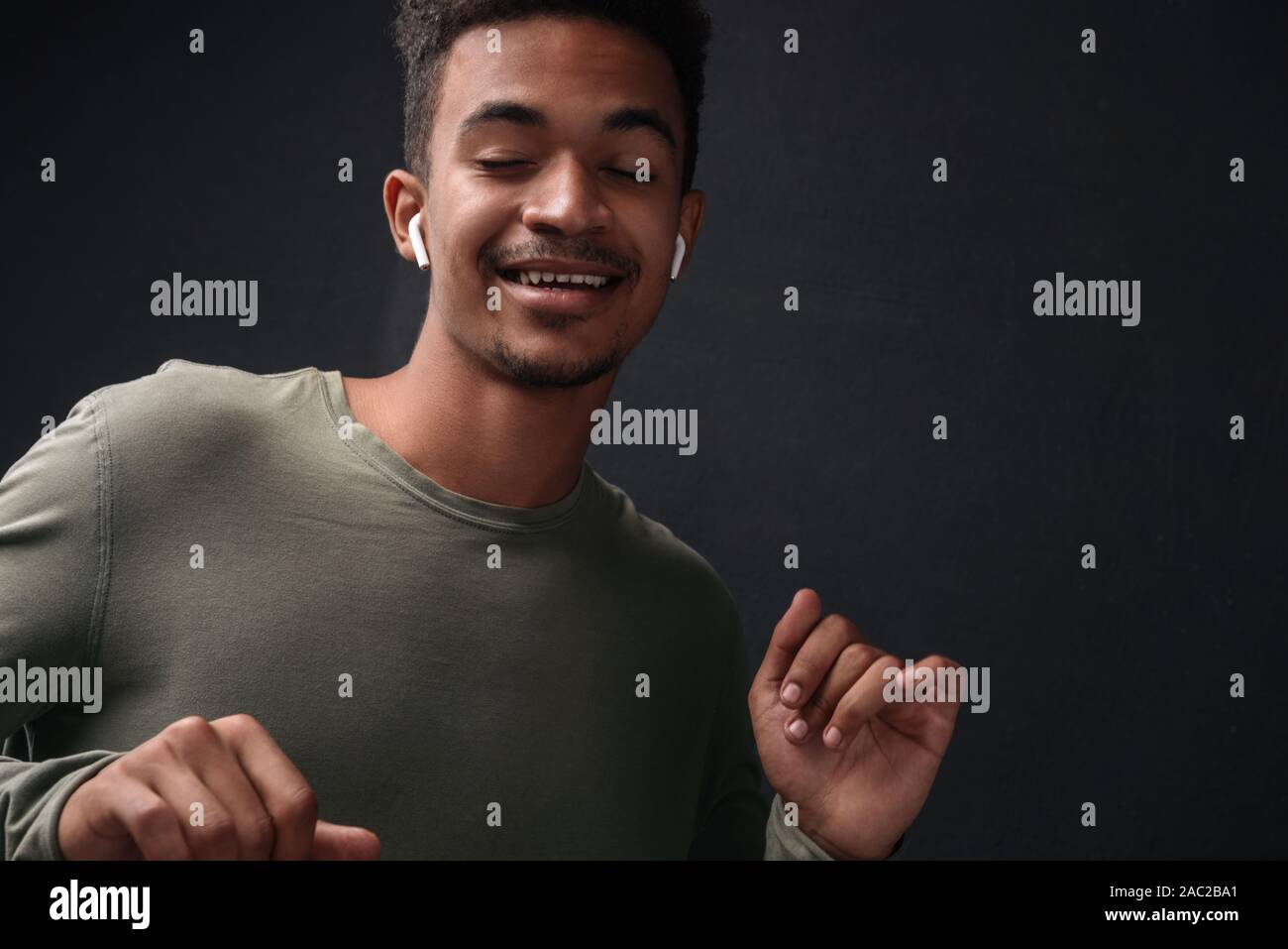 Image of happy african american guy with eyes closed using earpods and ...