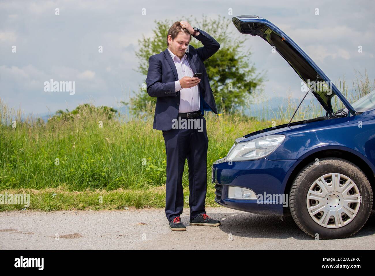 A broken car on the road, the driver is holding his head, an open hood ...