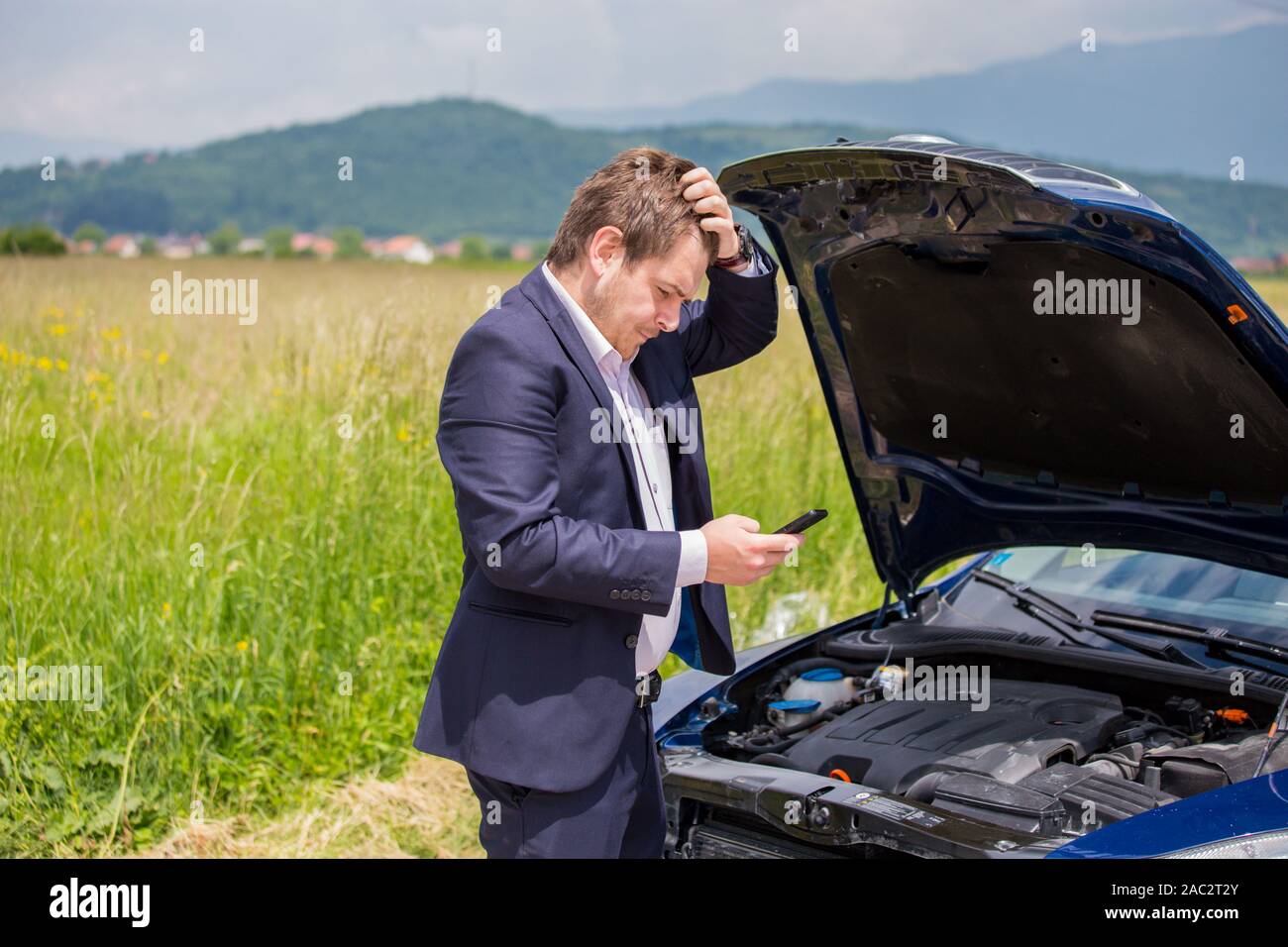 A broken car on the road, the driver is holding his head, an open hood ...