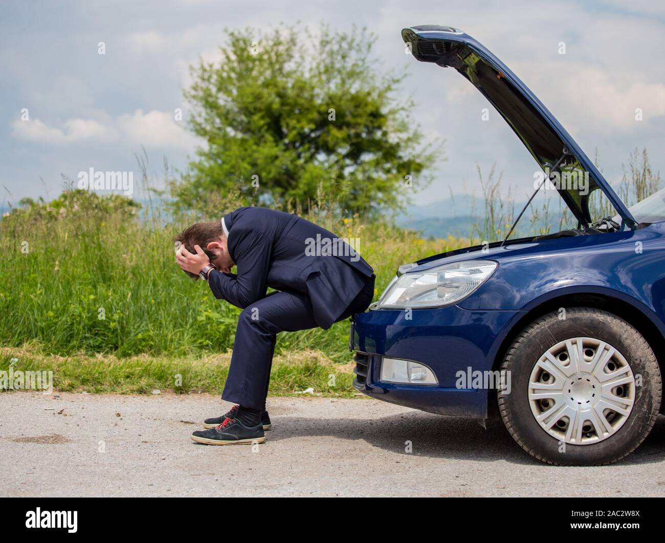 A broken car on the road, the driver is holding his head, an open hood ...