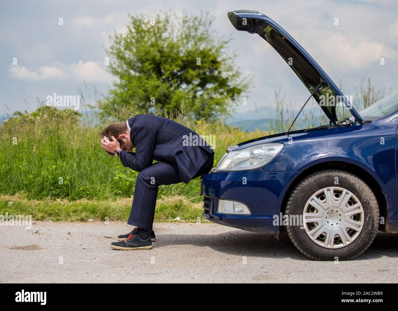 A broken car on the road, the driver is holding his head, an open hood ...